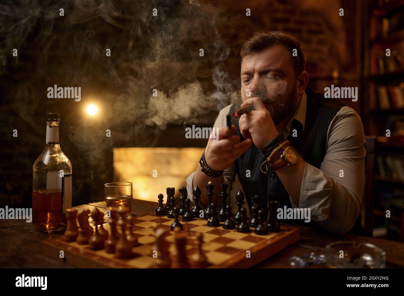 Man smokes a cigar, drinks alcohol beverage and play chess, bookshelf ...