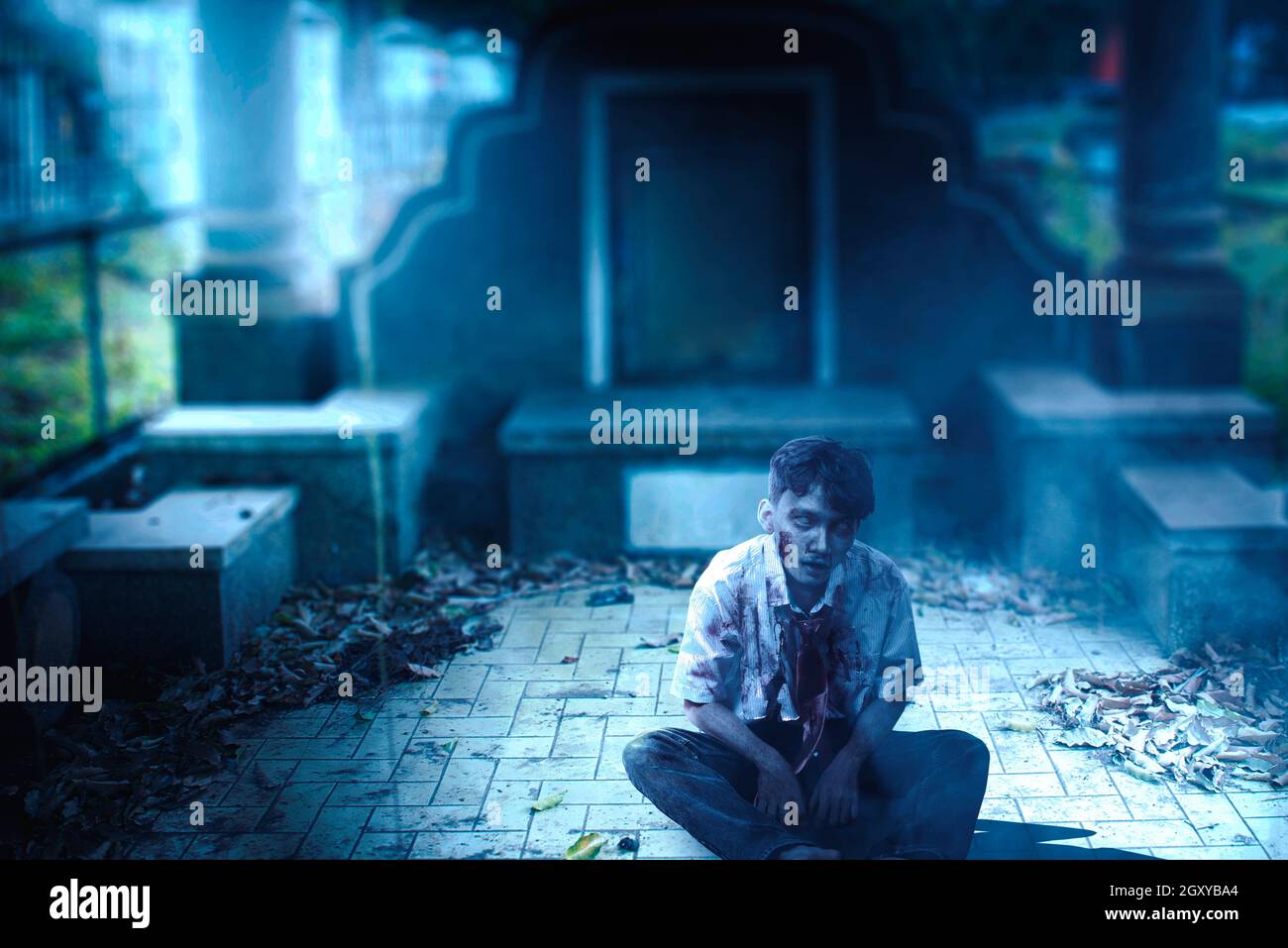 Scary zombie with blood and wound on his body sitting on the cemetery ...