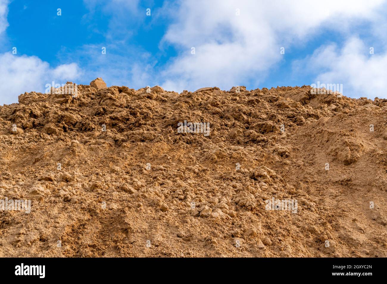 A large pile of sand for construction against a blue sky with clouds ...