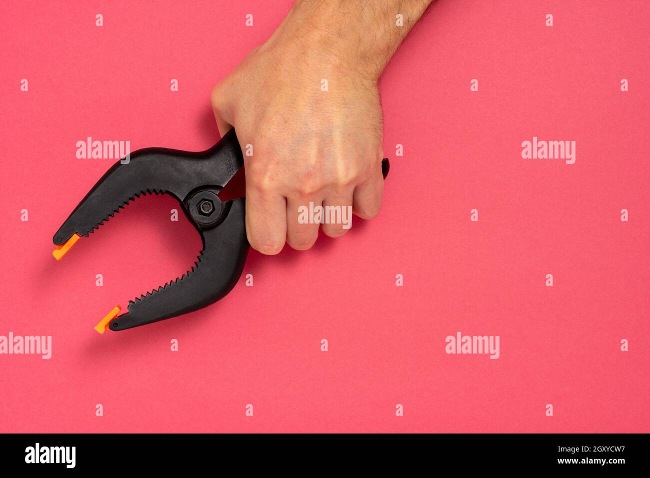 Hand holding large plastic spring clamp on pink background. Copy space ...