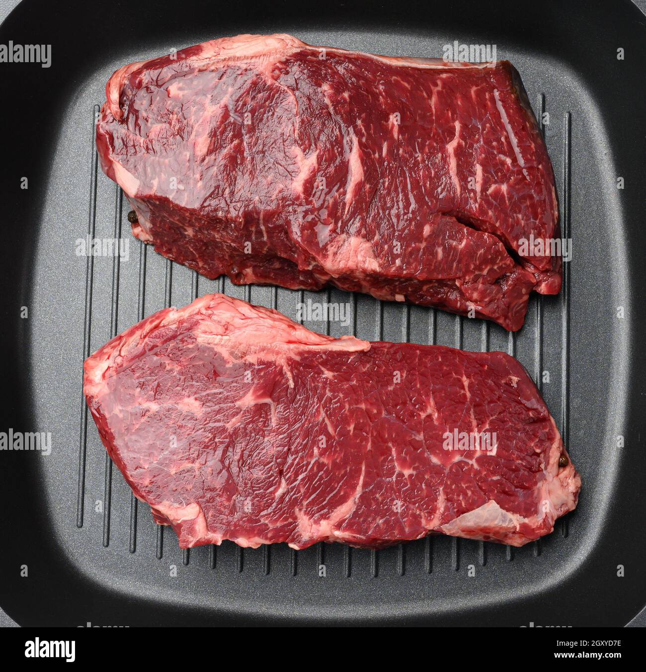 two raw pieces of beef in a black square grill pan, top view Stock ...