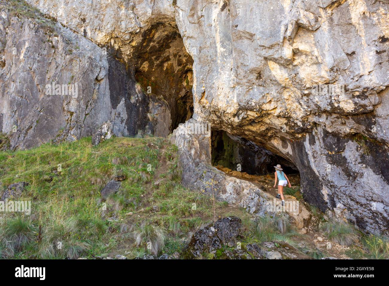 Female explorer entering a cave system in mountainous terrain in ...