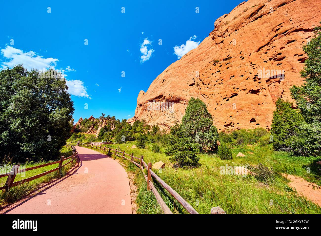Paved walking path with fence through desert with large red mountain ...