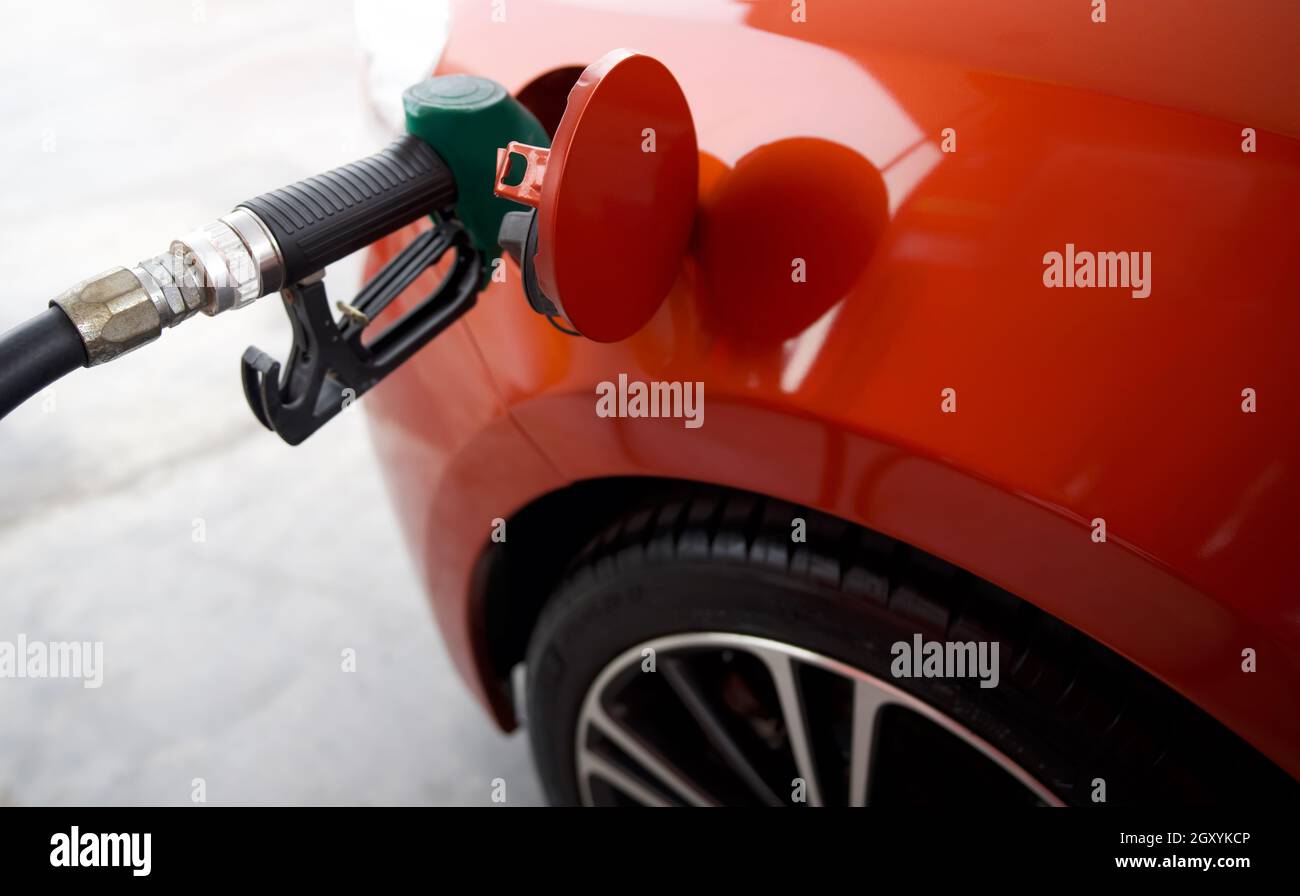 Green benzene gas pump nozzle filling up orange sport car tank. Close ...