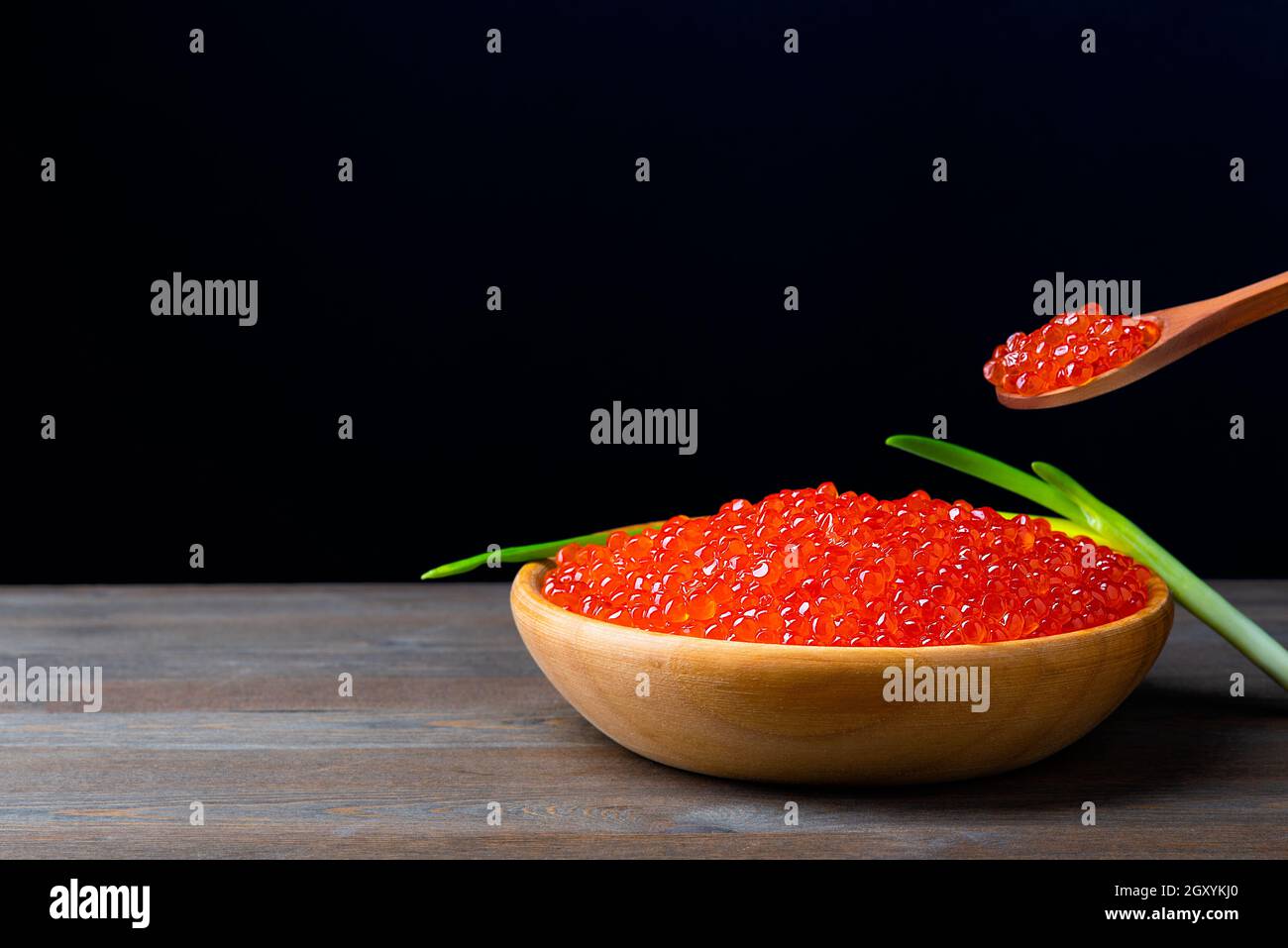 Red caviar in a wooden cup on a black background with a spoon and green ...