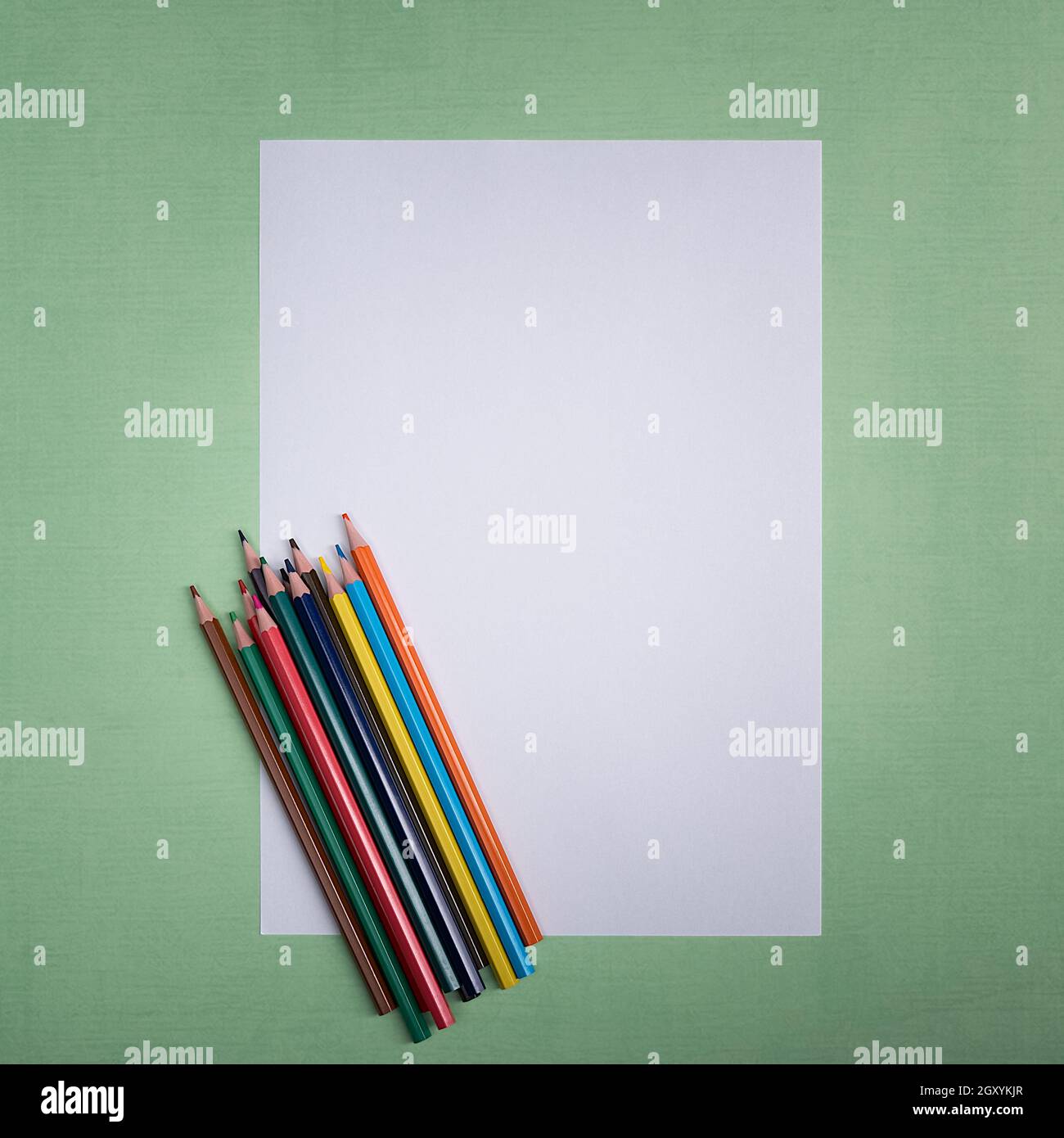 A blank white sheet and colored pencils for drawing on a plain textured ...
