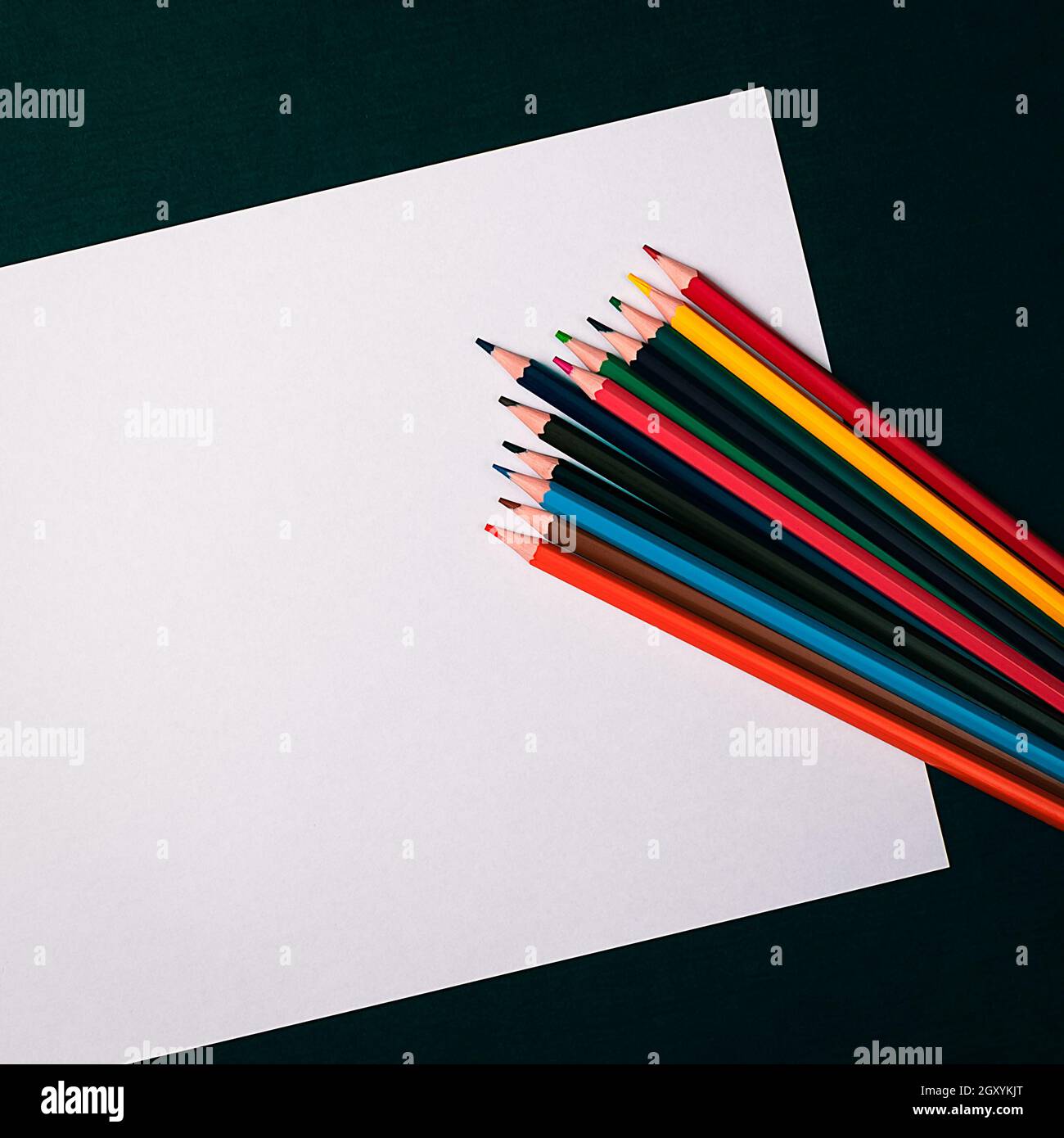 A blank white sheet and colored pencils for drawing on a plain textured ...