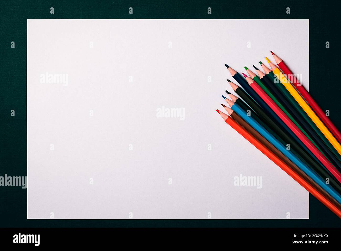 A blank white sheet and colored pencils for drawing on a plain textured ...