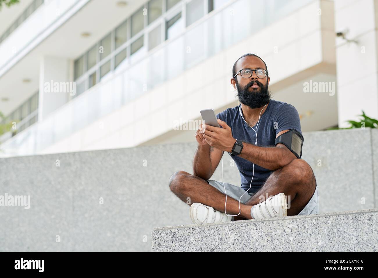 Calm young Indian man with beard sitting with crossed legs on concrete ...