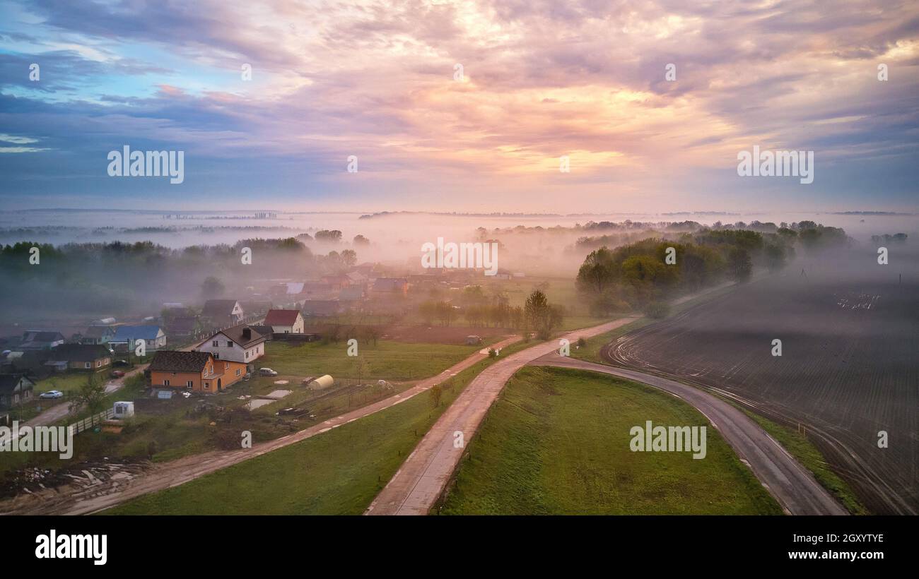 Aerial view of village, rural dirt road and trees covered by fog. Early ...