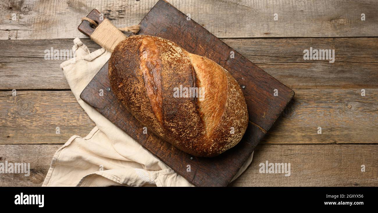 whole oval baked bread on a brown cutting board, top view Stock Photo ...