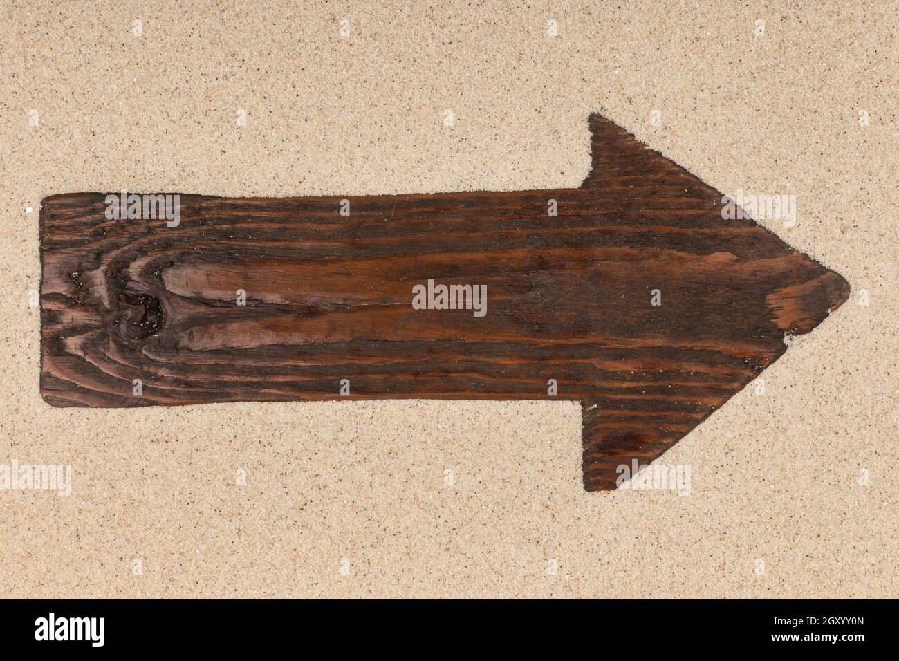 Classic arrow made of dark wood lies in the sand. With space for text ...
