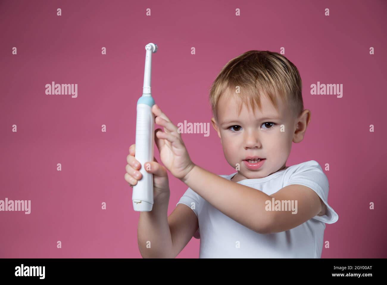 Smiling caucasian little boy holds electric sonic toothbrush on pink ...