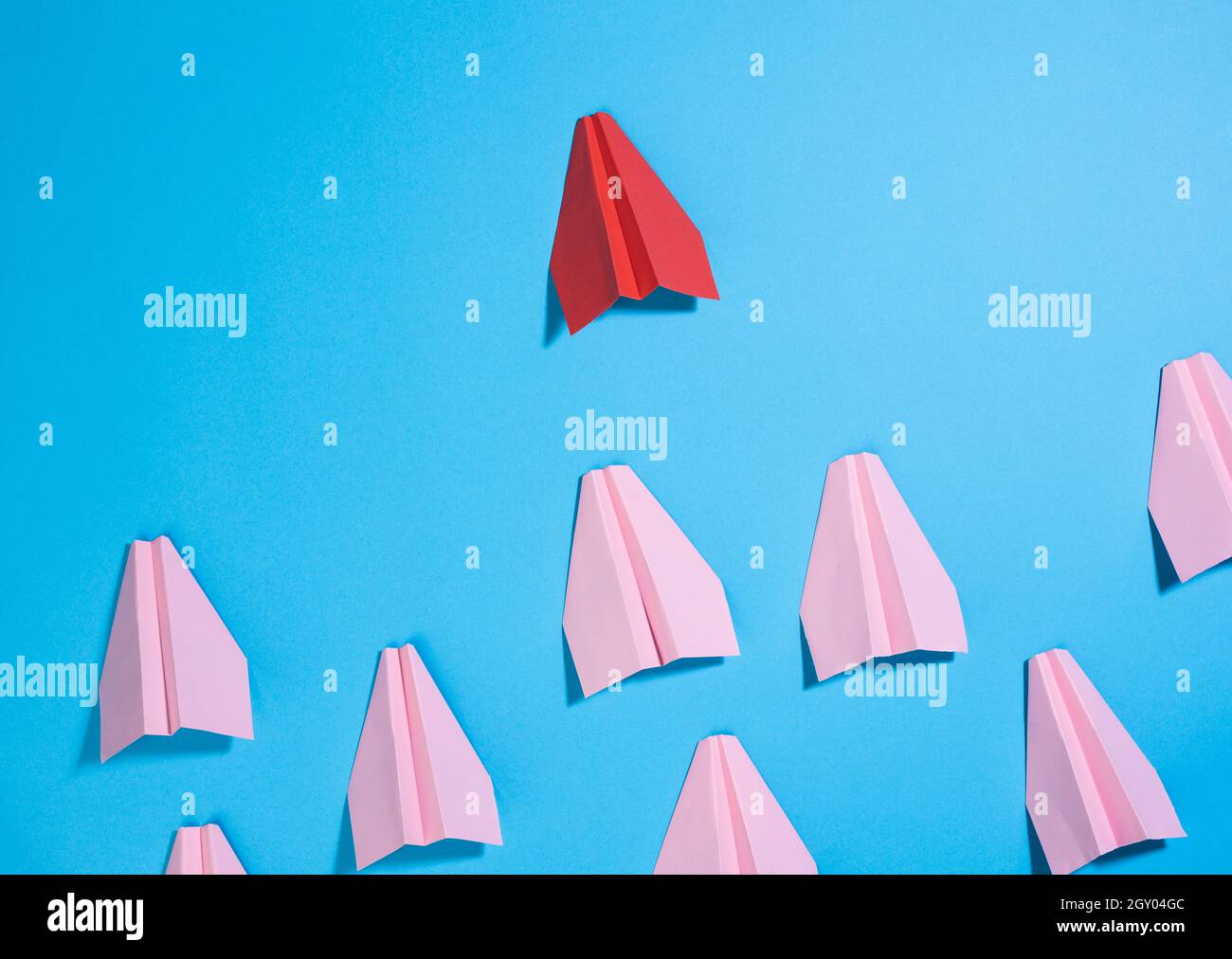 group of pink paper planes follow the first red against a blue ...