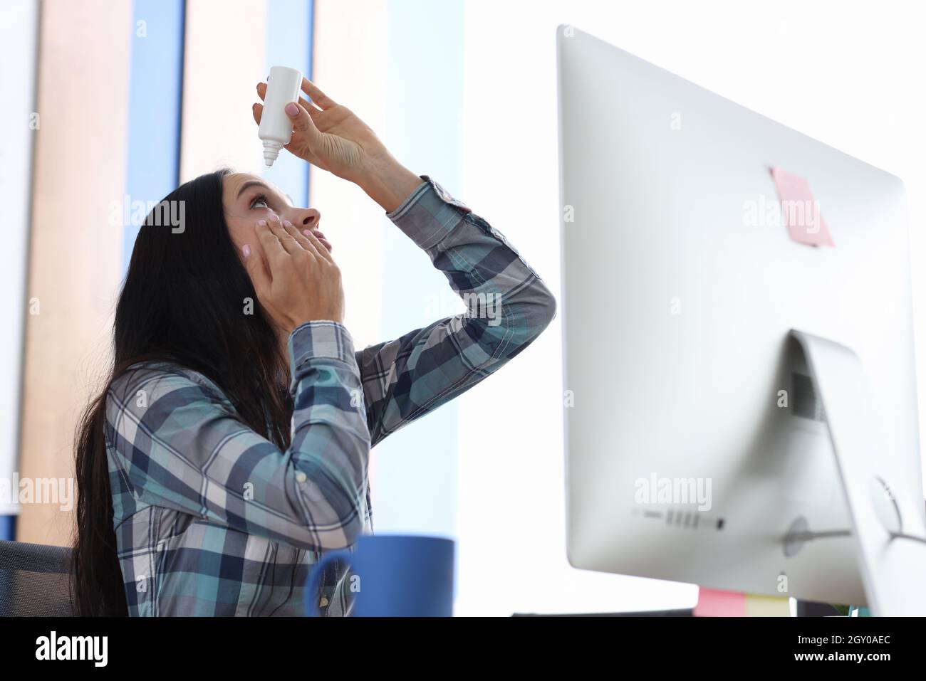 Woman drips eye drops into eyes while sitting at workplace at computer ...