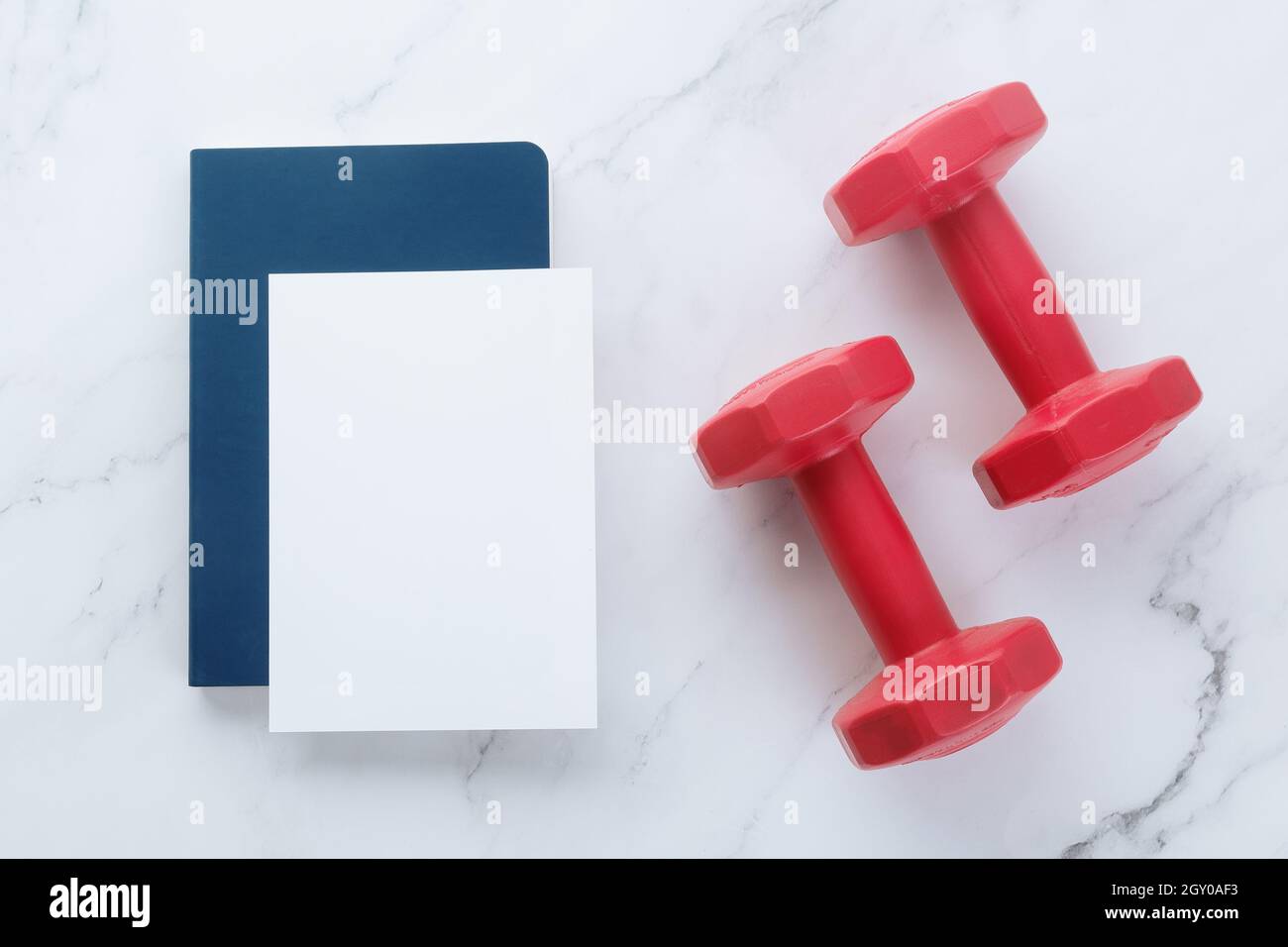 Blank white paper note and dumbells on white marble background. Sport ...