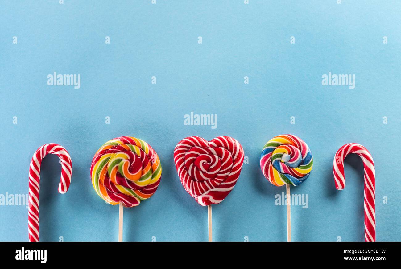 A colorful line of tasty rainbow lollipops on wooden sticks with blue ...