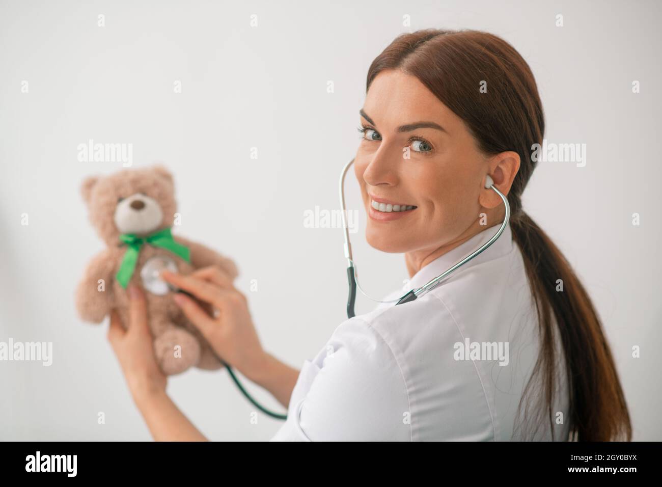 Smiling doctor performing an auscultation procedure on a teddy bear ...
