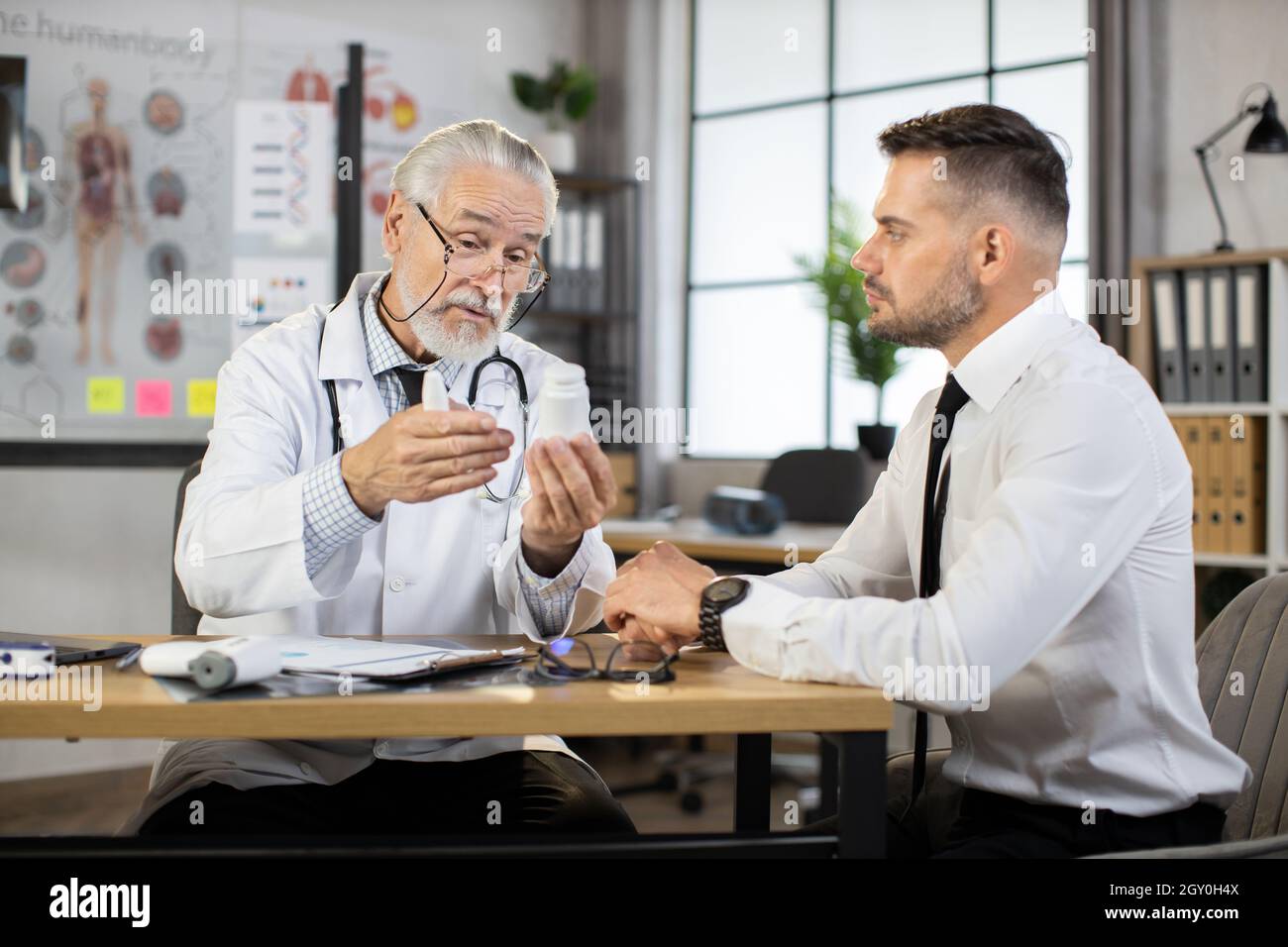 Mature medical worker in eyeglasses and lab coat prescribing medication ...