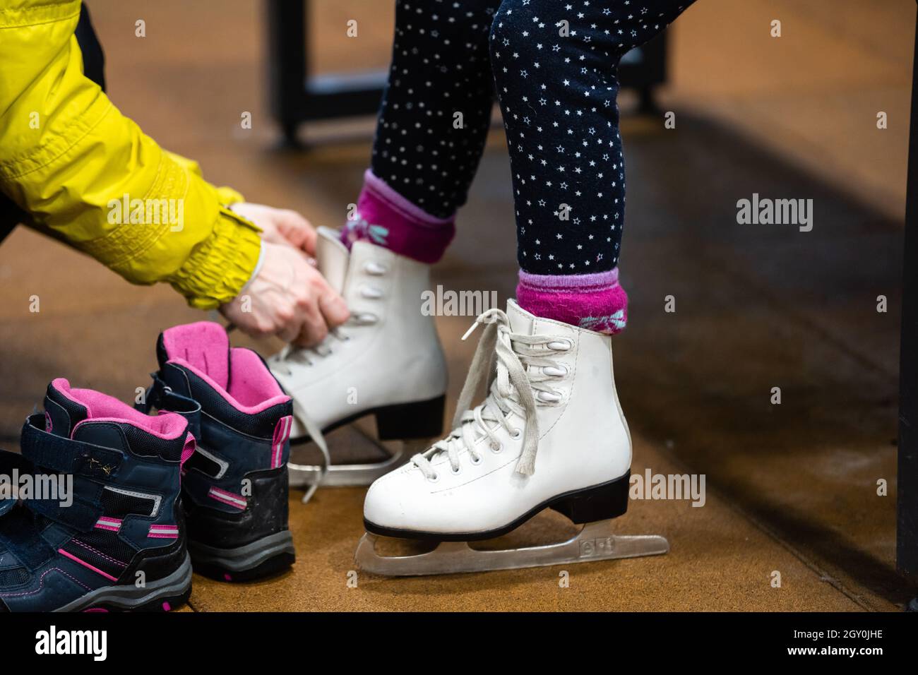 Woman is helping her daughter put her figure skates on before she takes ...