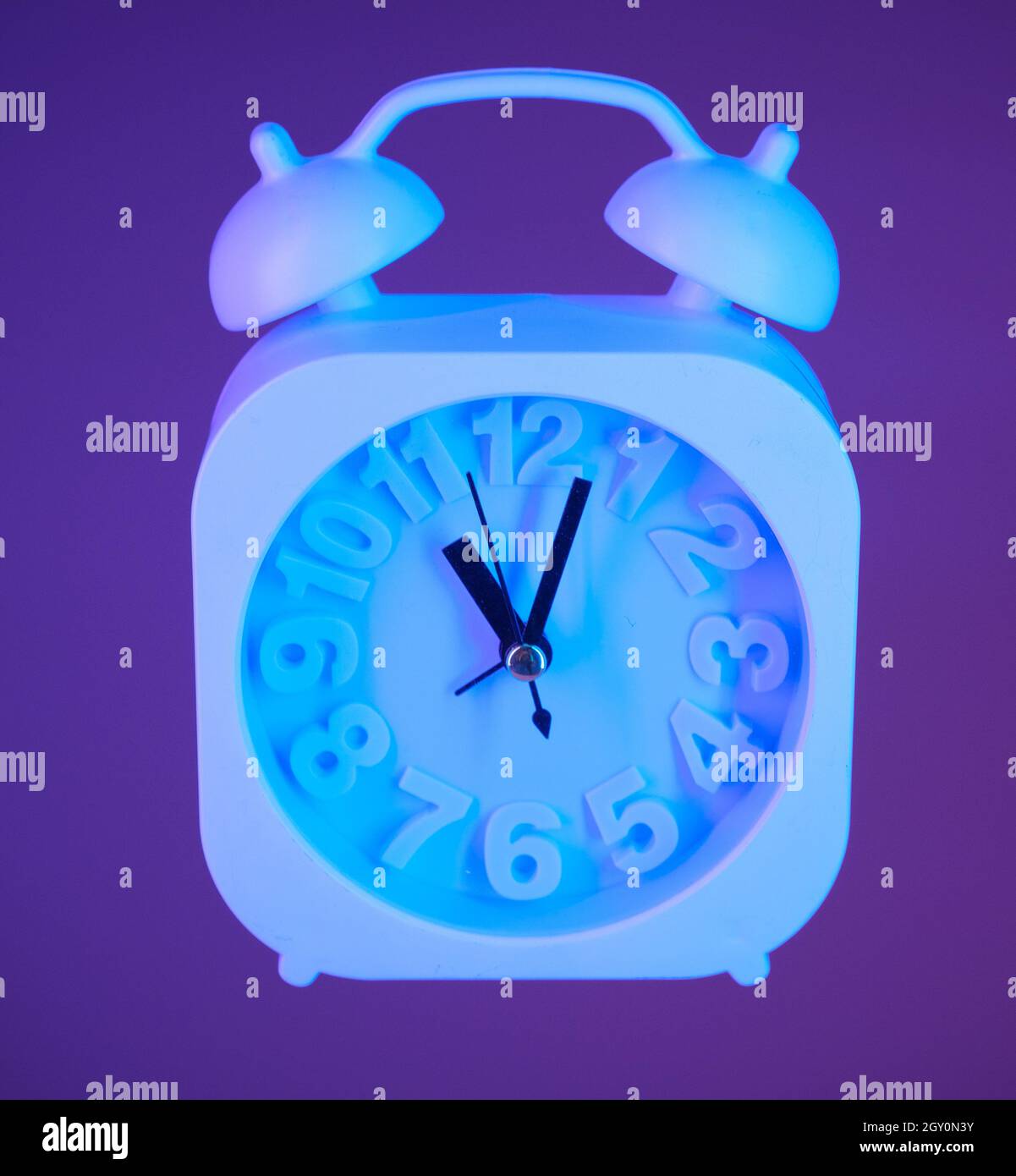 Light blue alarm clock suspended in air on a bright purple background ...