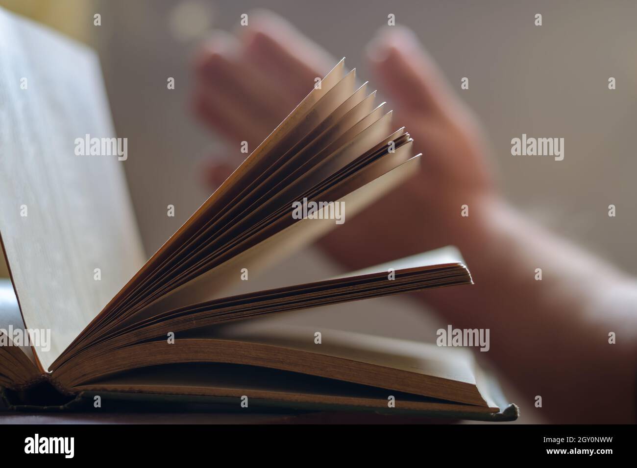 Defocused shot of an old open book and two men's hands. Palms folded to ...