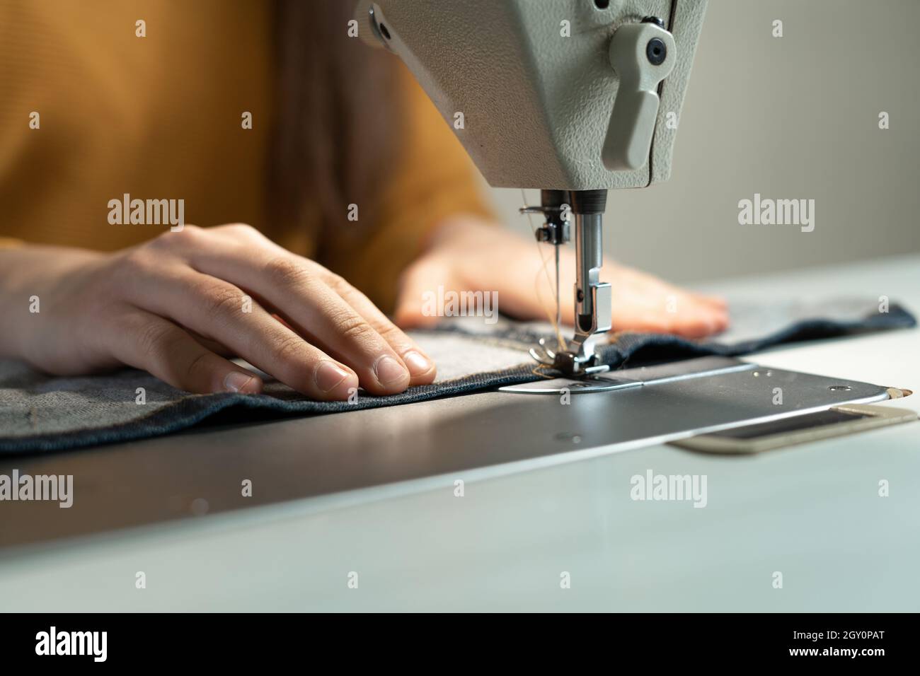 The girl's hands put the fabric under the needle in the sewing machine ...