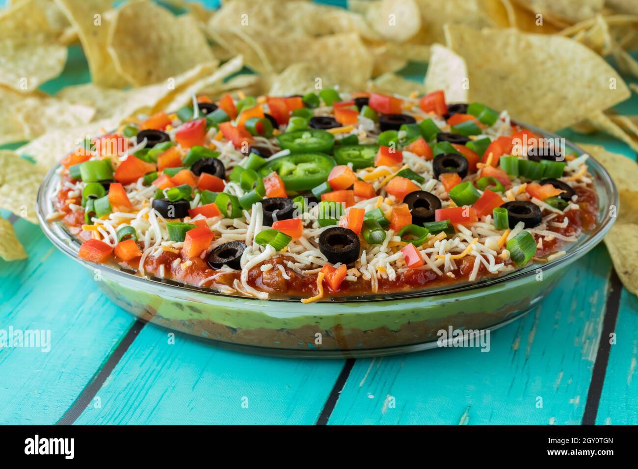 Close up of a freshly made Mexican layered dip, with chips in behind ...