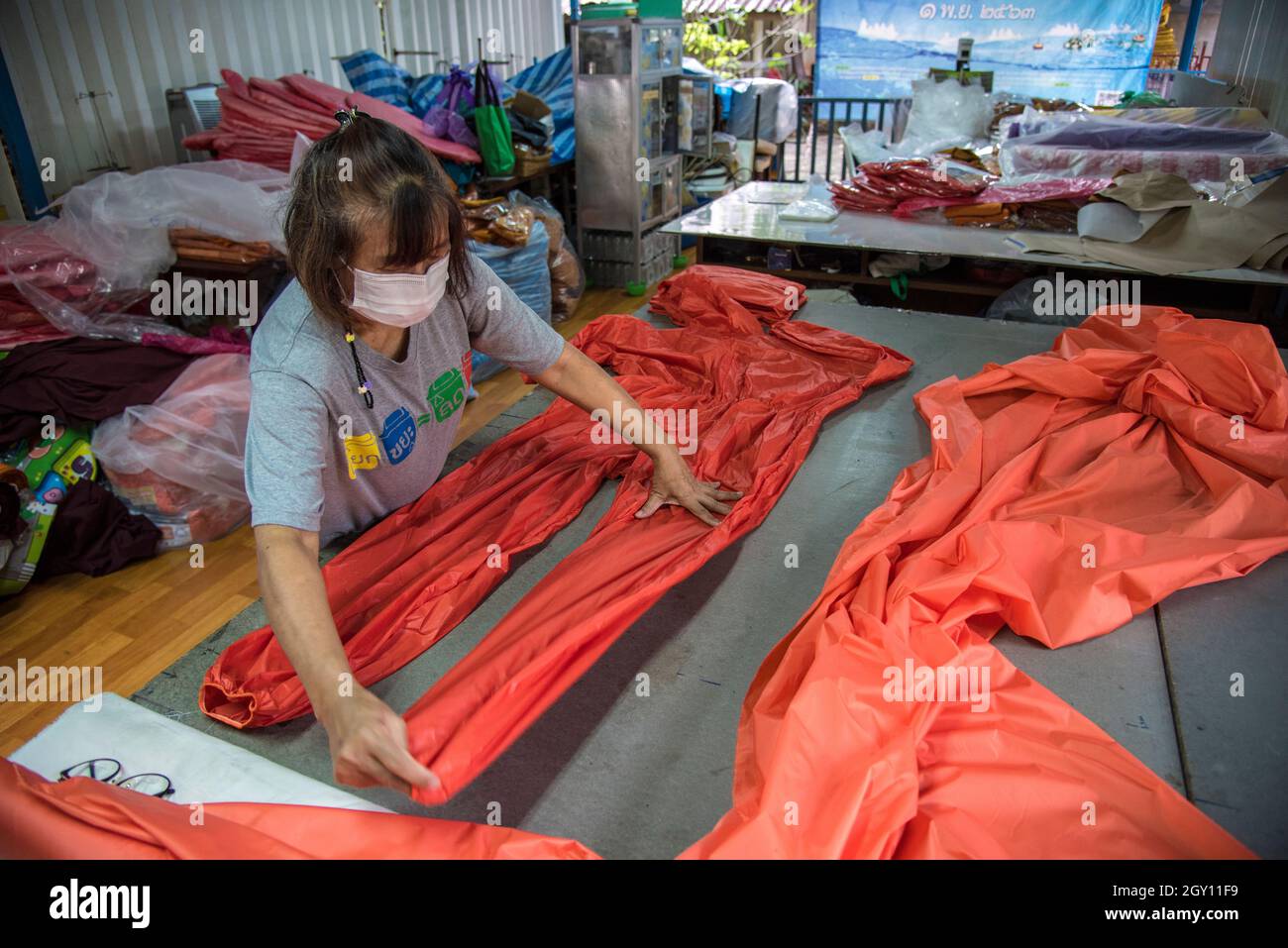 A woman sews a a personal protective equipment suit (PPE) for Buddhist ...