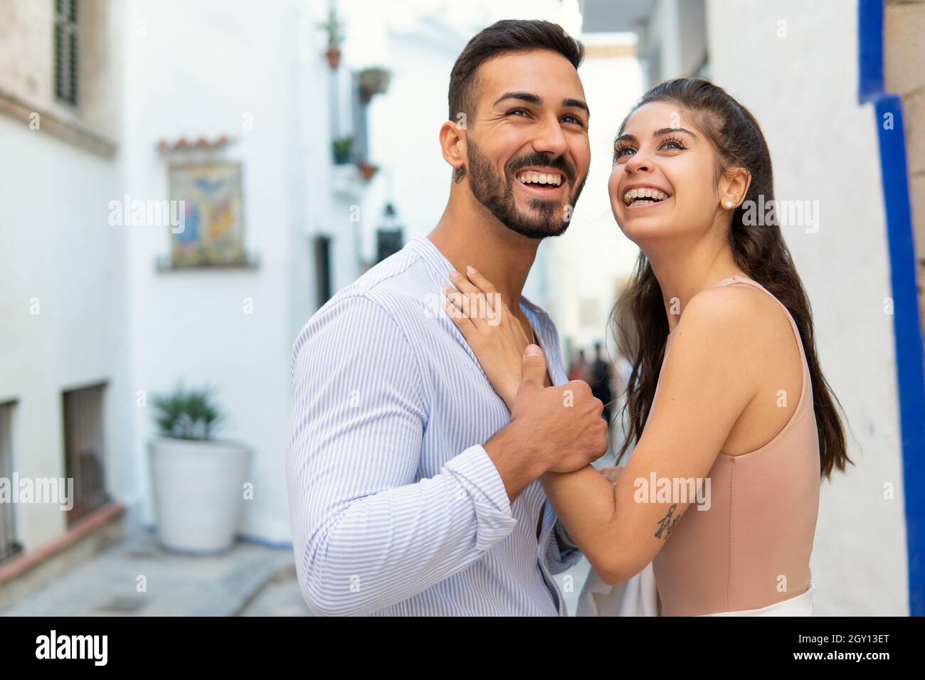 Side view of carefree ethnic couple in stylish clothes cuddling on ...