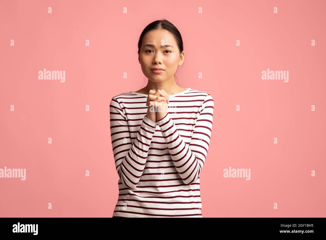 Please. Young asian female begging with clasped hands and looking at ...