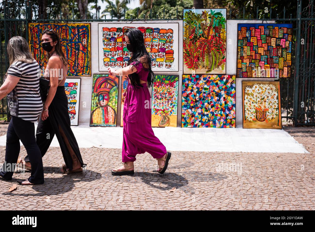 Women walking by a display of art paintings for sale at the Belo ...