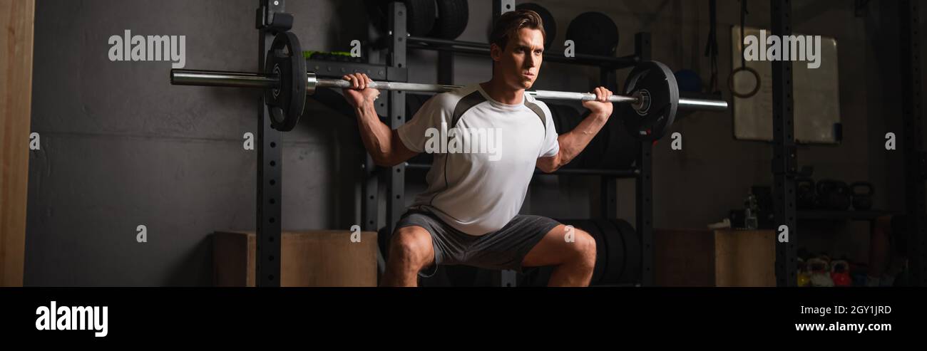 concentrated man working out with barbell in sports center, banner ...