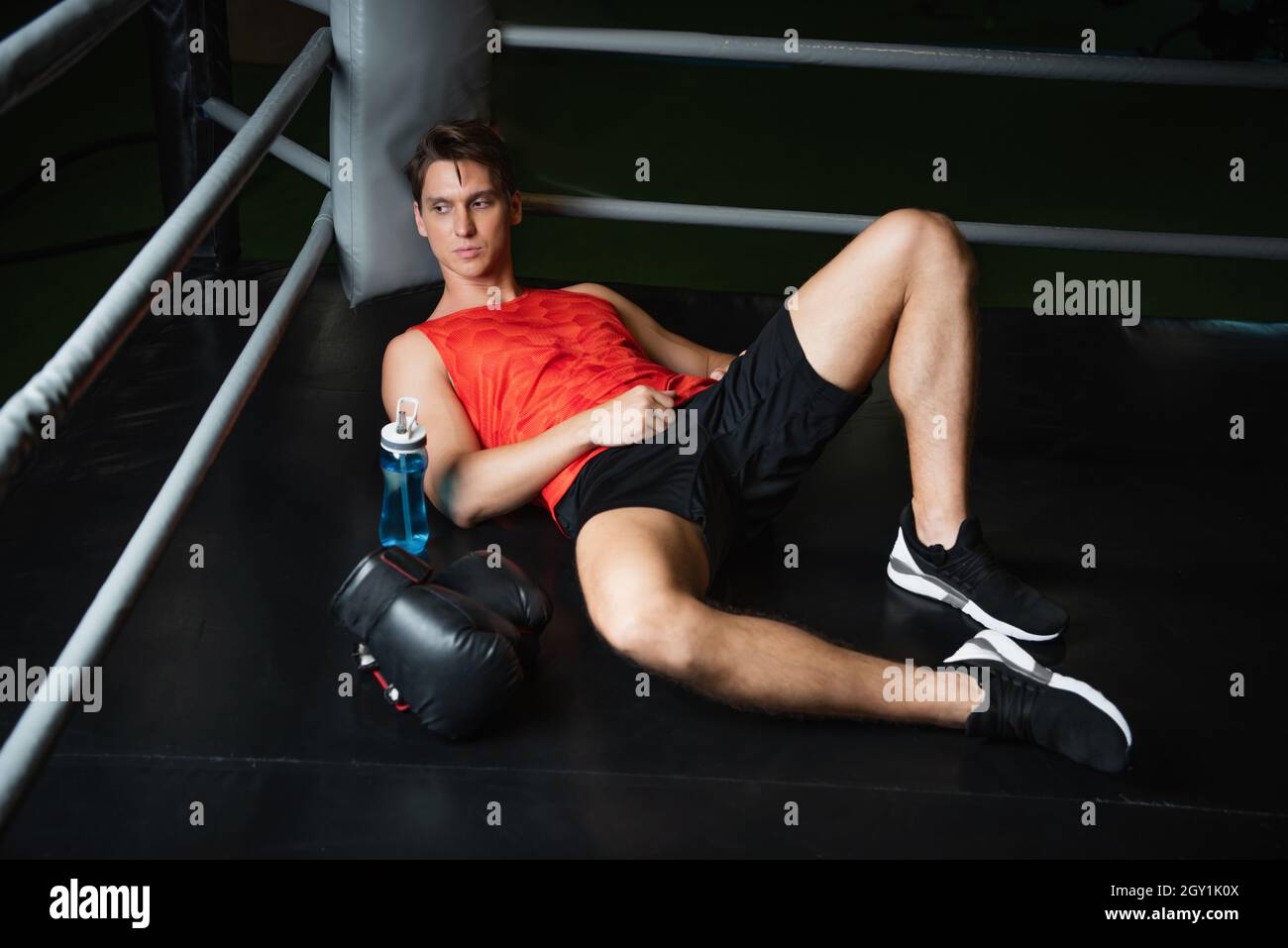 tired sportsman resting in corner of ring near boxing gloves and sports ...