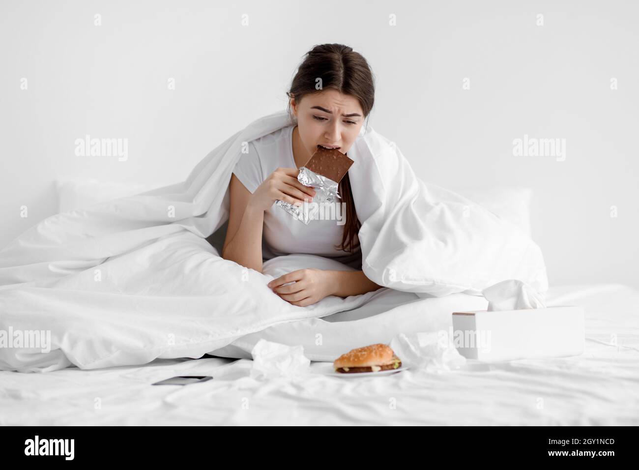 Sad hungry european millennial female eating big chocolate bar sitting ...