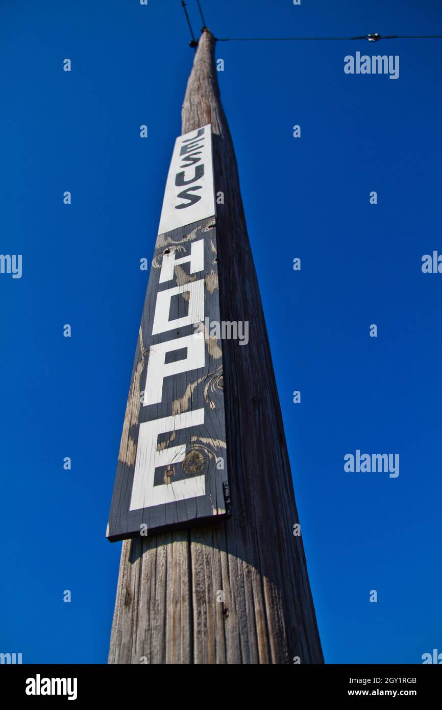 Tall wooden telephone pole with a black and white sign saying Jesus ...