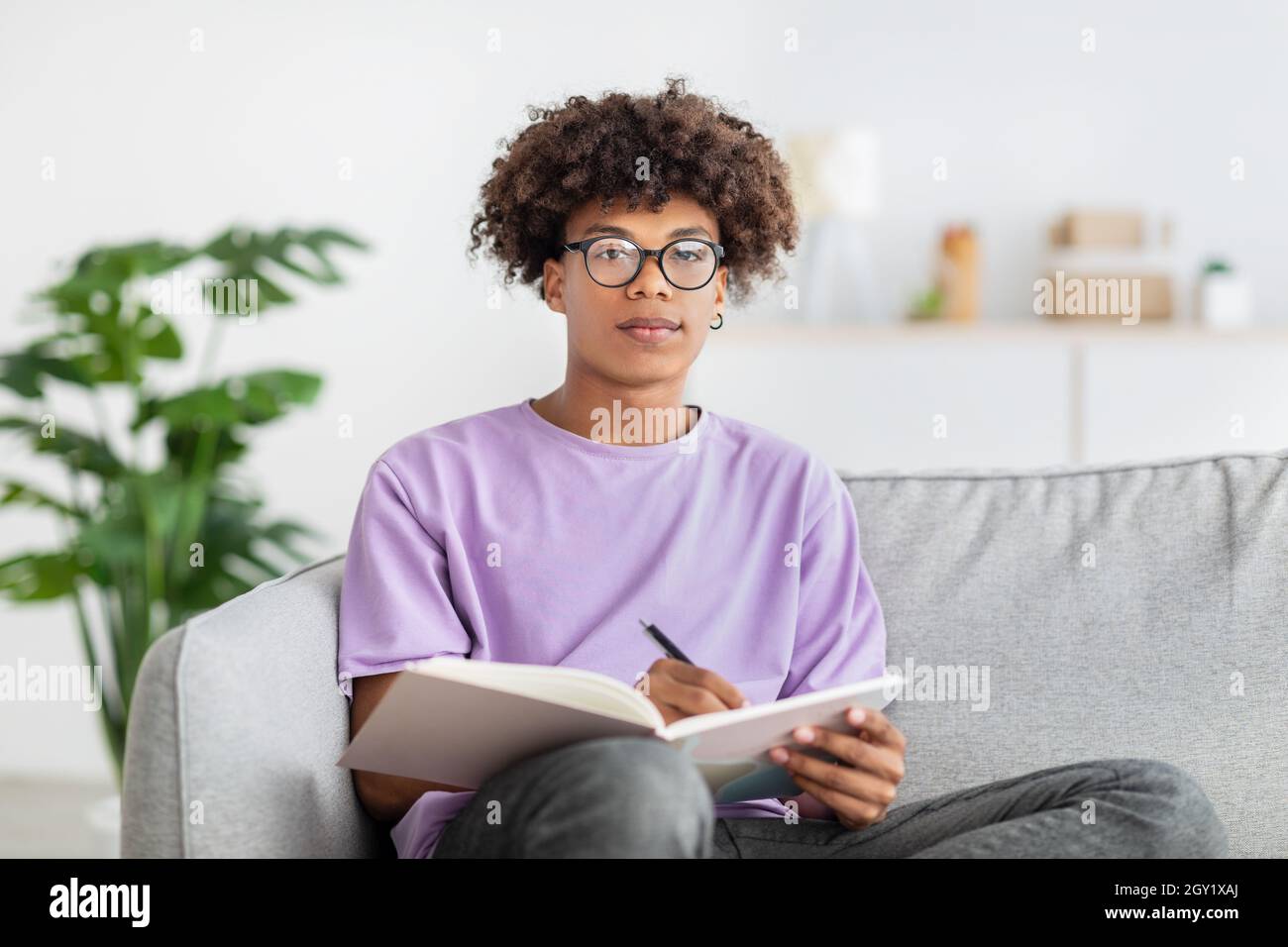 Focused black teenager writing in notebook, getting ready for exam or ...