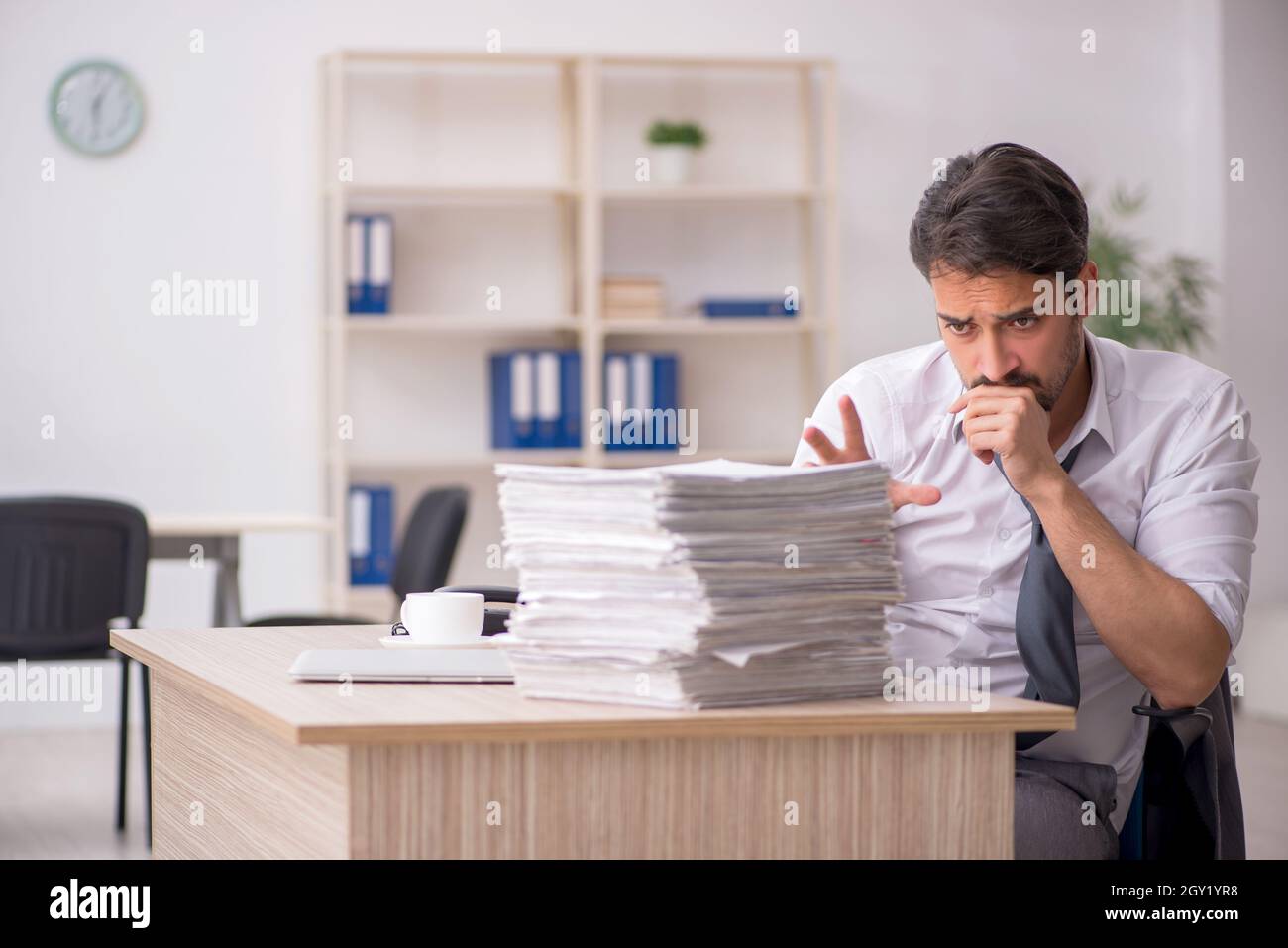 Young male employee and too much work at workplace Stock Photo - Alamy