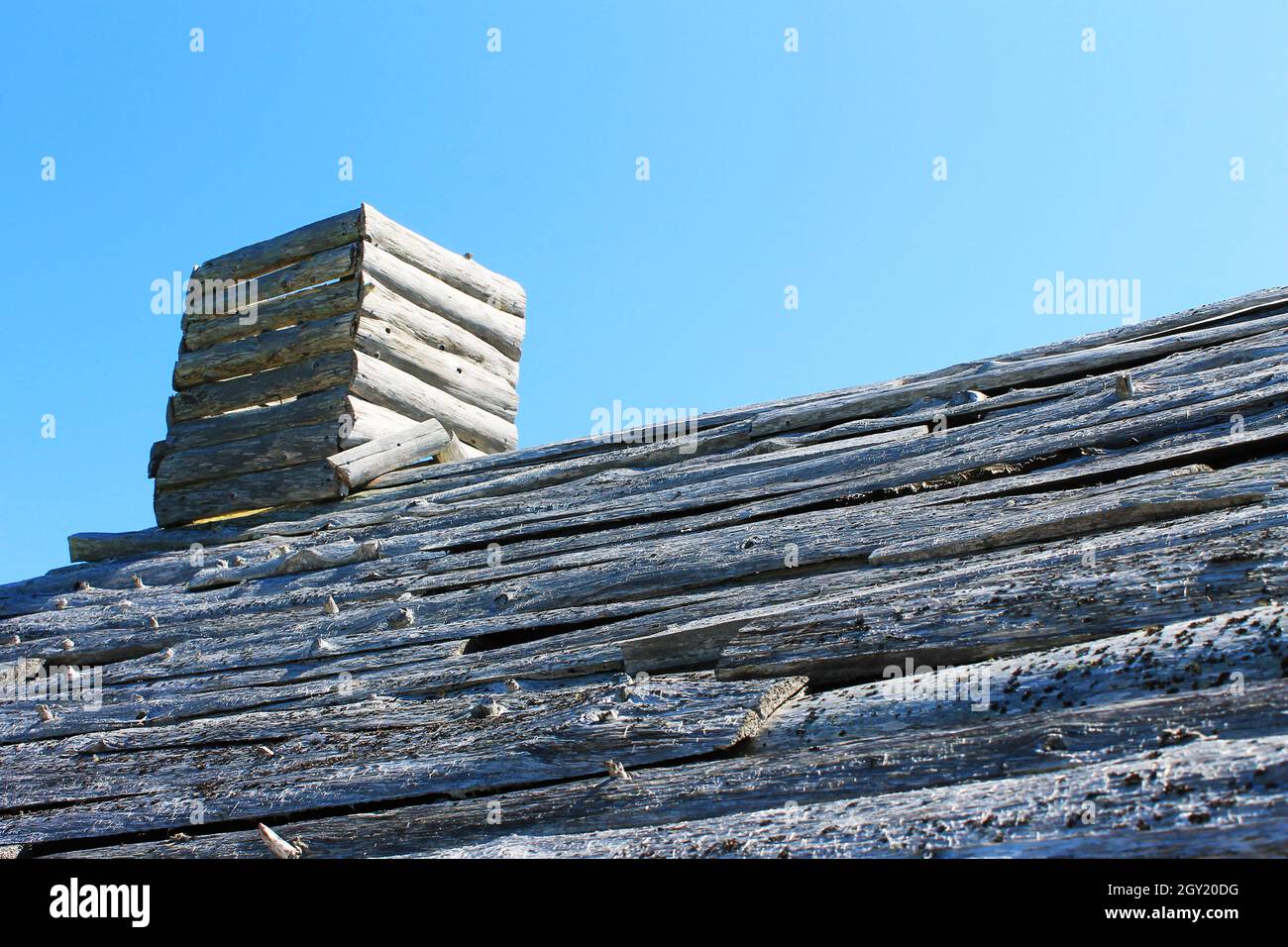 A close-up of a gray and weathered, split log roof and chimney. clear ...