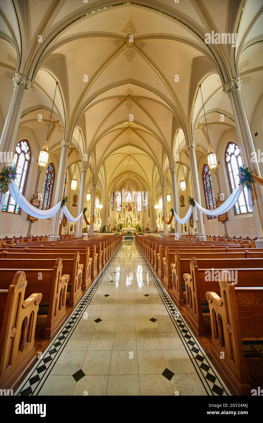 White interior of a large cathedral that shows the pews leading to the ...