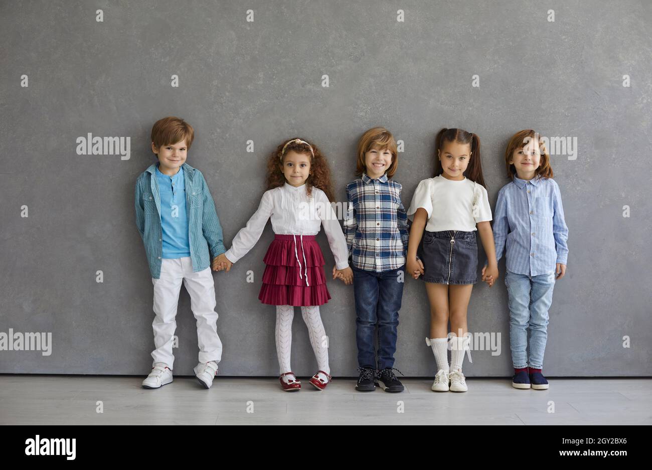 Smiling little children group stand in row against studio wall looking ...