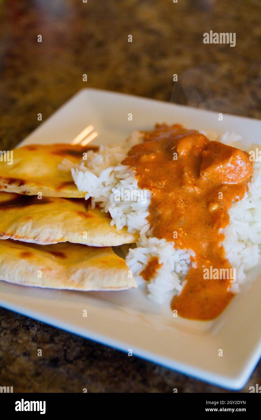 Indian dinner of orange curry or butter chicken over rice with fresh ...