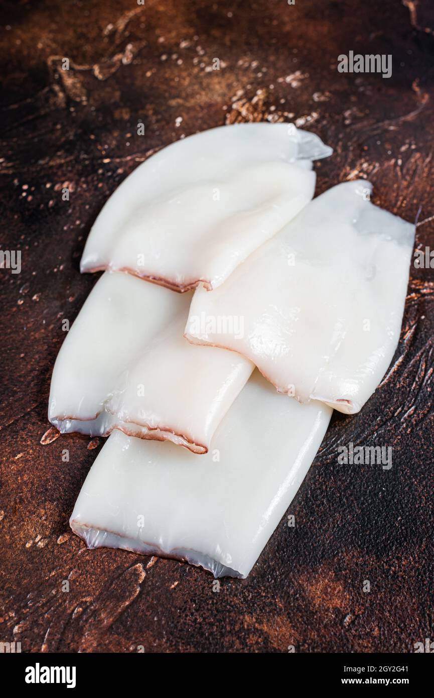 Raw Squid or Calamari tubes on a kitchen table. Dark background. Top ...