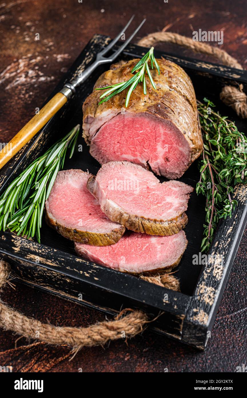 Roast beef round fillet meat in a wooden tray with herbs. Dark ...