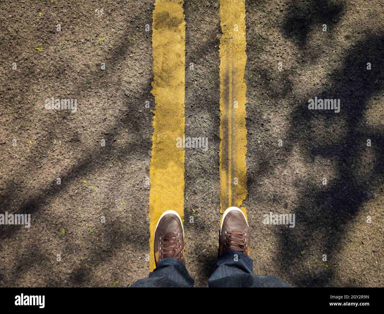 Top view of male feet on two yellow lines on asphalt with tree shades ...