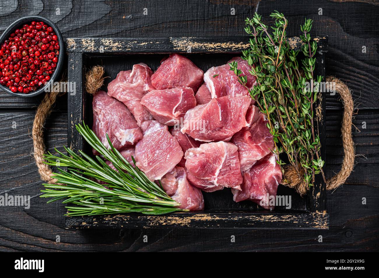 Raw Diced pork cubs meat with spices in a rustic tray. Black wooden ...