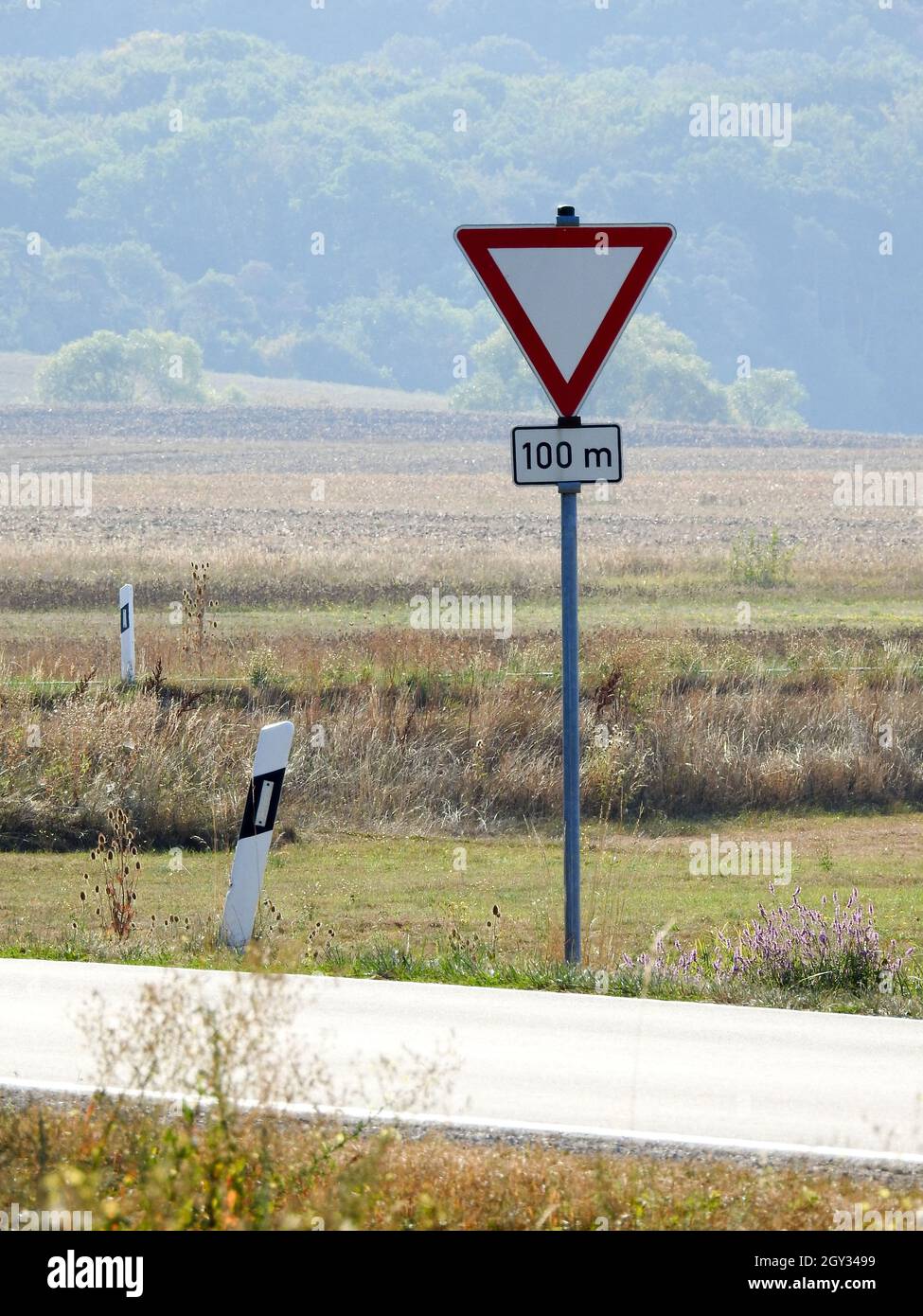 Vertical shot of a roadside warning sign of "give way in 100 meters ...