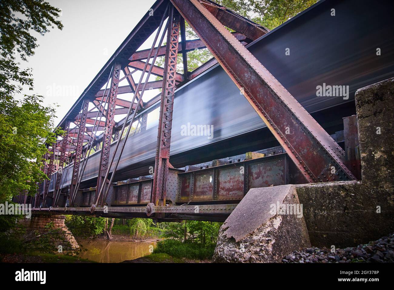 Old metal train track bridge over river with blur of train crossing ...