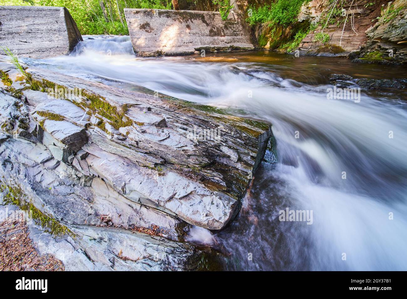 Cement dam funneling river with large outcropping of stone covered in ...