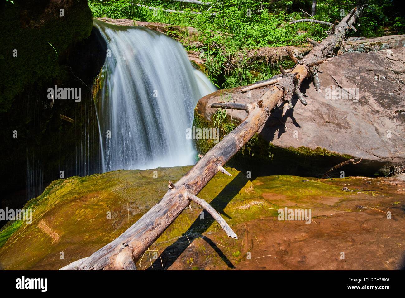 Waterfall over rocks with long log Stock Photo - Alamy